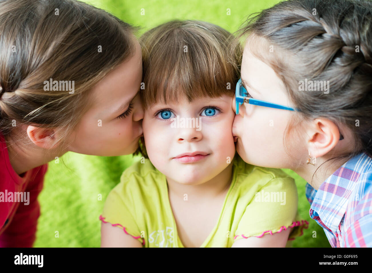 Embarrassed little girl kissed by two sisters Stock Photo - Alamy