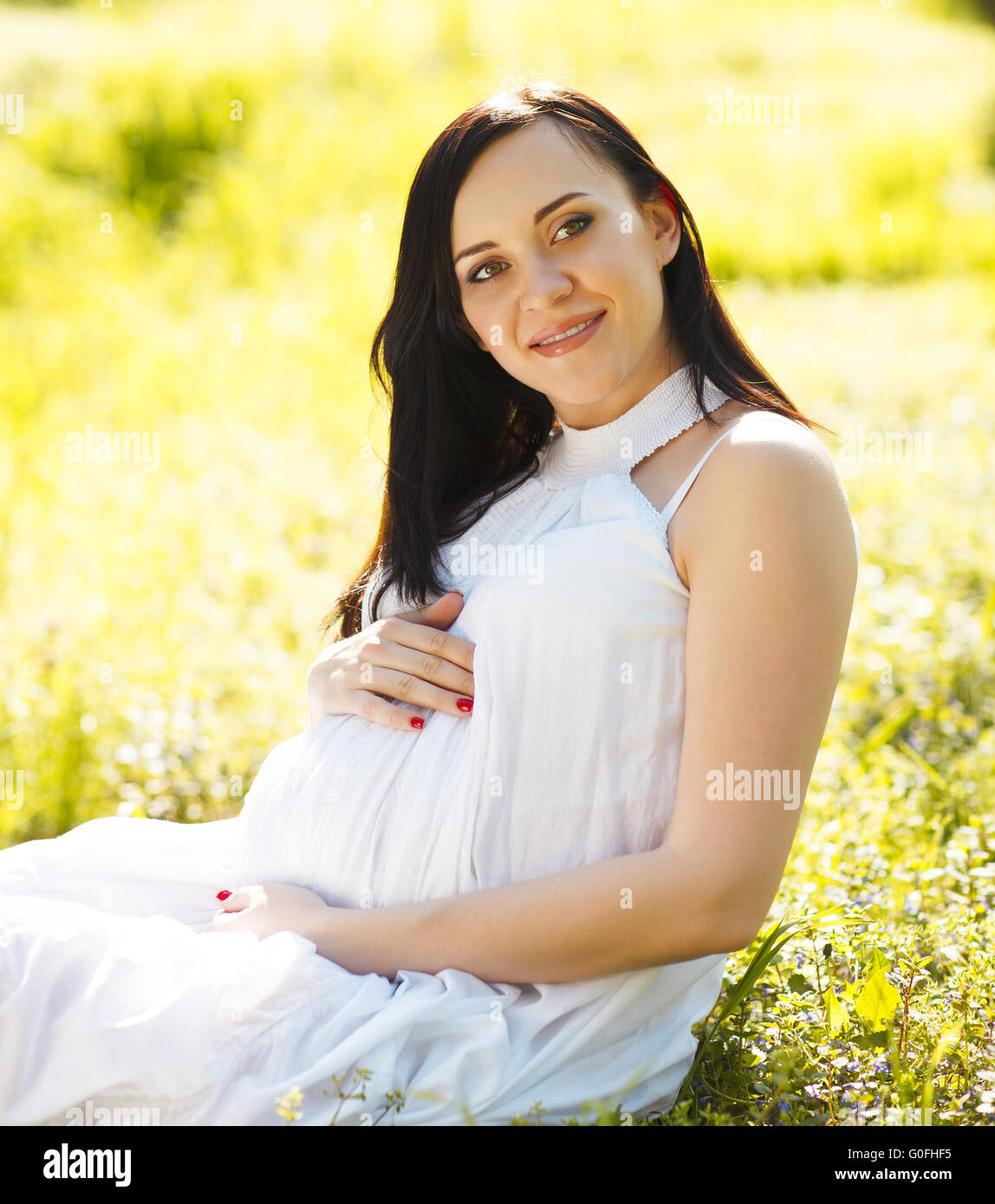 Beautiful pregnant woman in white dress in the flowering spring park ...