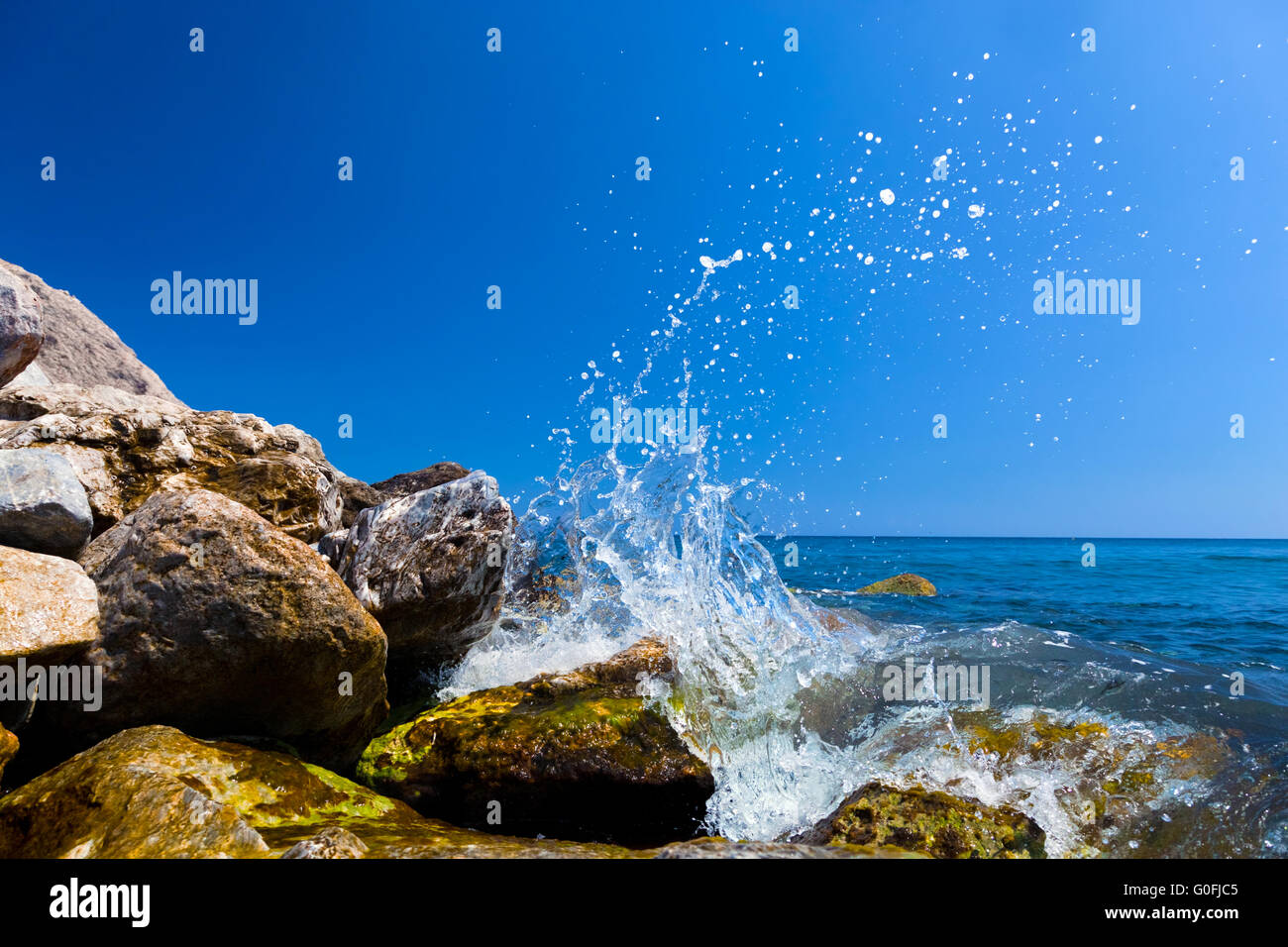 Waves hitting rocks on a tropical beach forming a splash shape. Greece ...