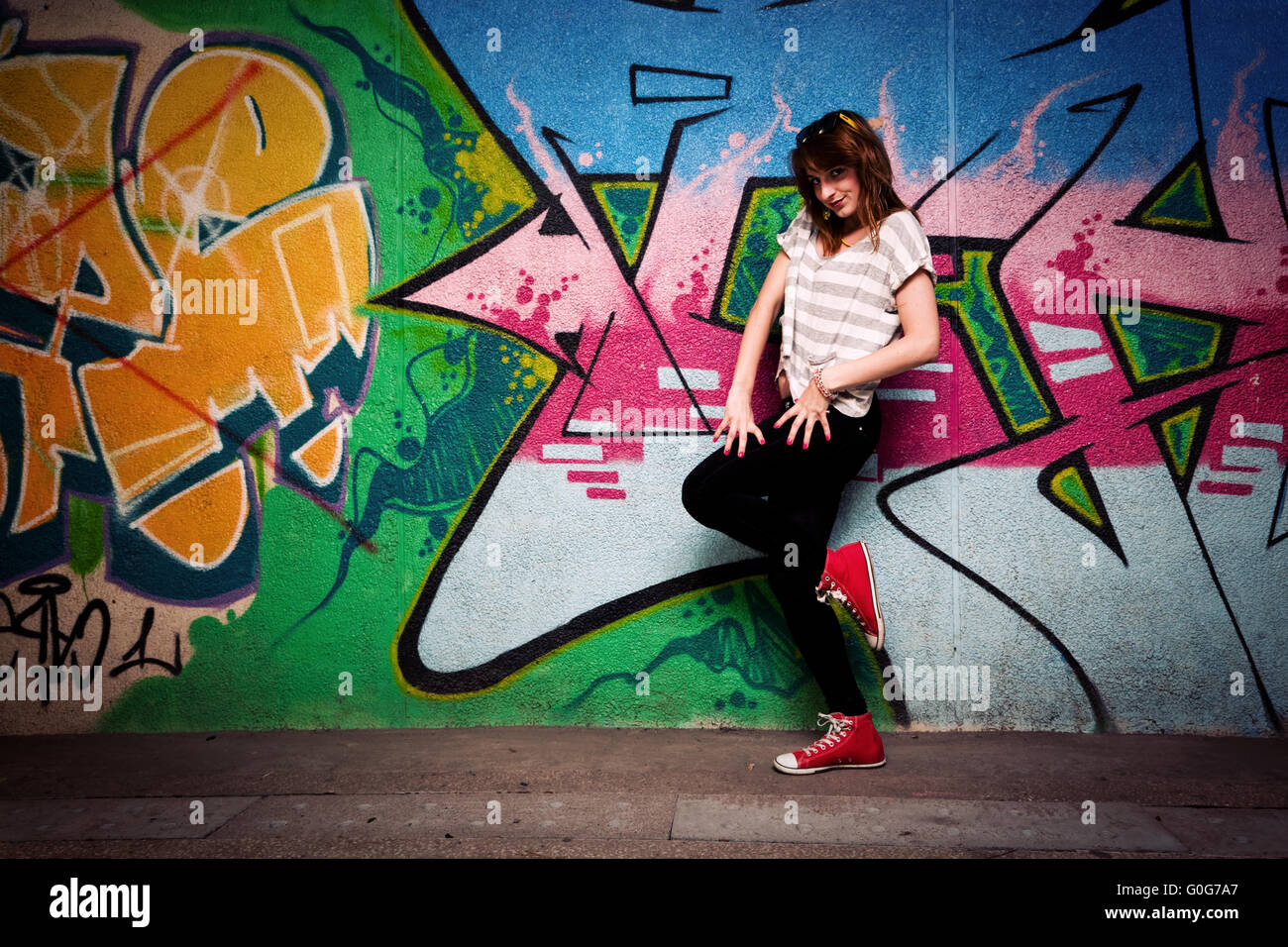 Stylish fashionable girl in a dance pose against colorful graffiti wall ...