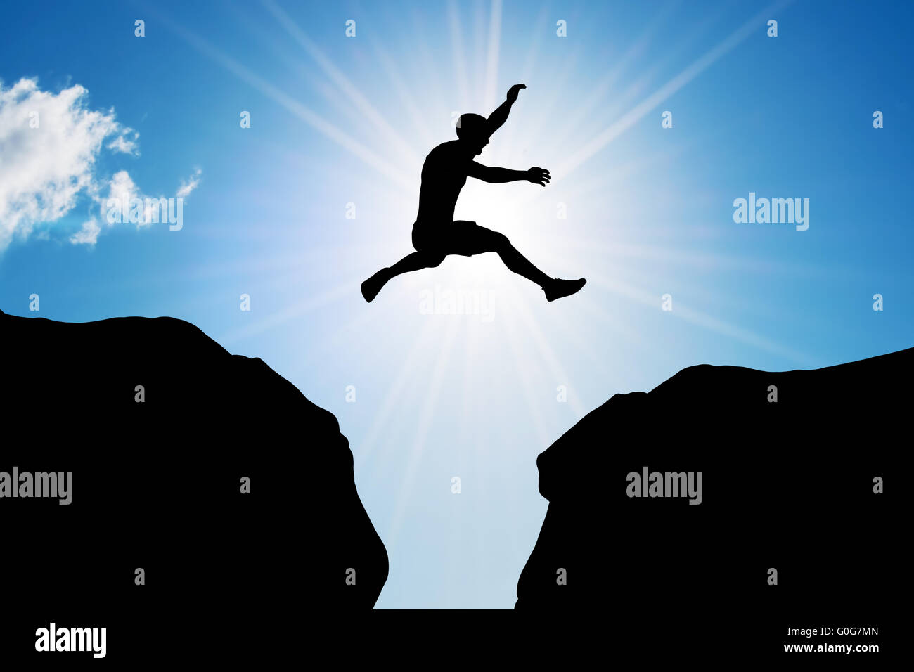 Man jumping over precipice between two rocky mountains at sun light ...