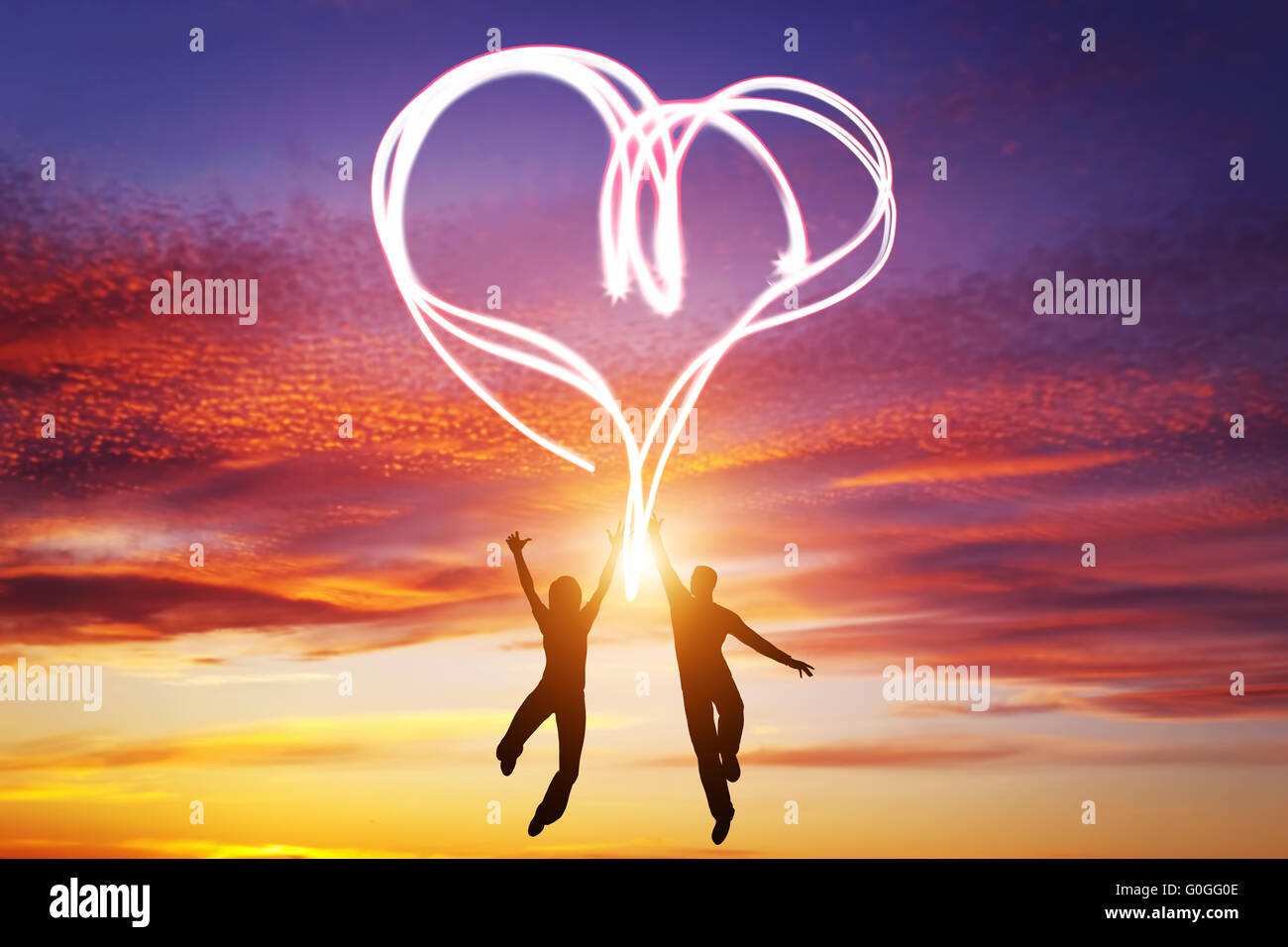 Happy couple jump together and make a heart symbol of light manifesting ...