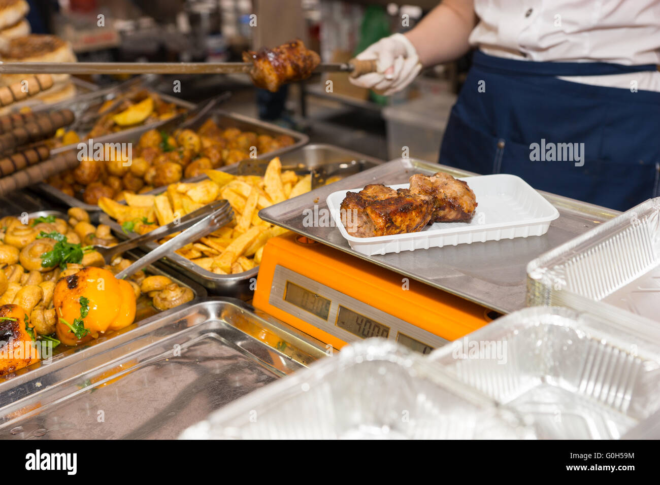 Unidentifiable food server in blue apron using metal skewer to place ...