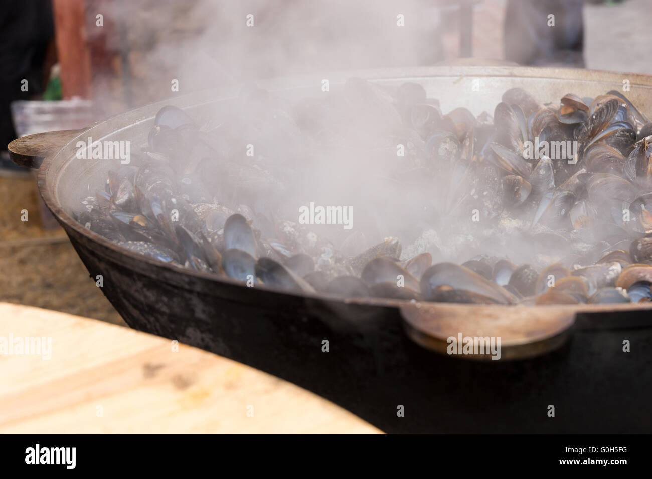 Mussels steaming in a large commercial open-air steamer over hot coals ...