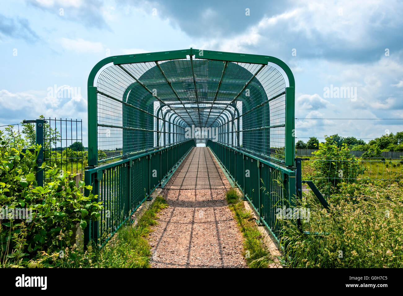 A pink gravel path leads to a footbridge protected by green safety ...