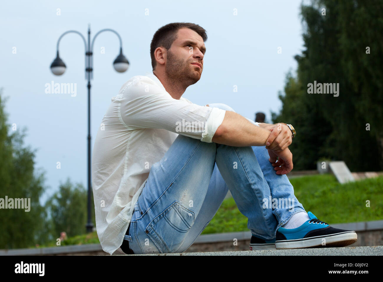 Young tired man sit on border in summer park Stock Photo - Alamy