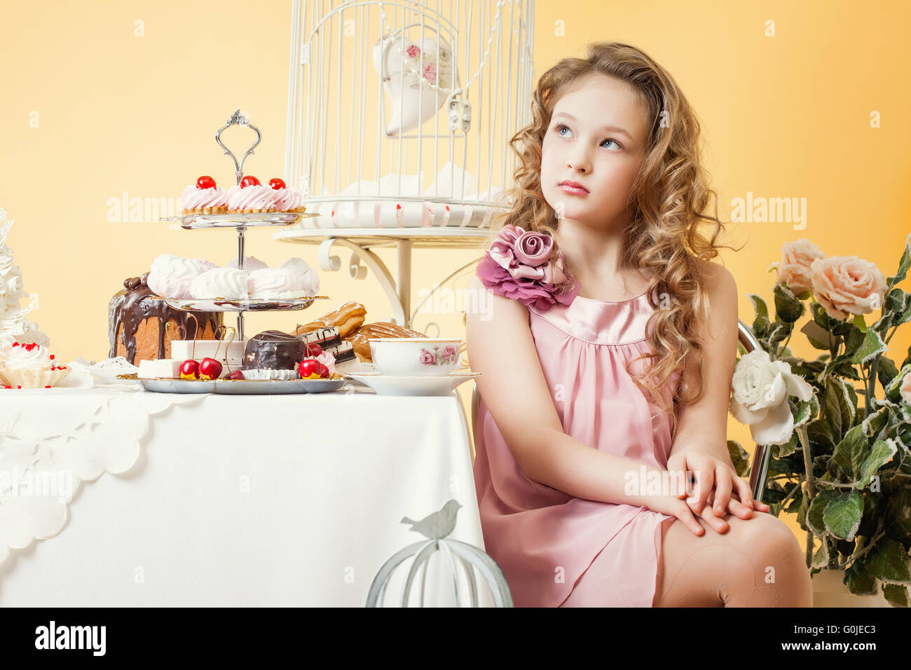 Thoughtful little lady posing at table with cakes Stock Photo - Alamy