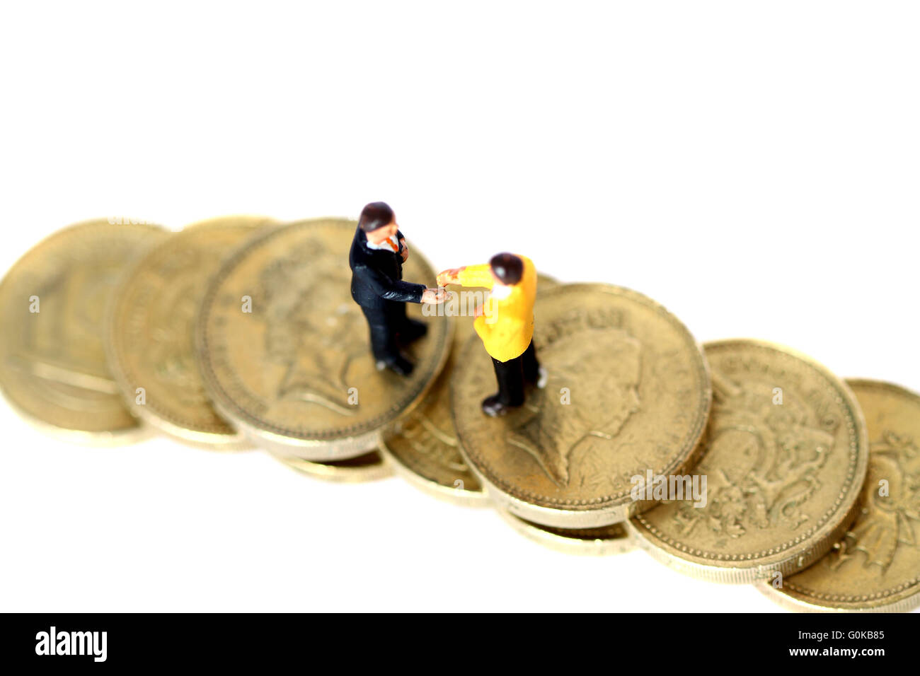Miniature businessmen shaking hands on pound coins Stock Photo - Alamy