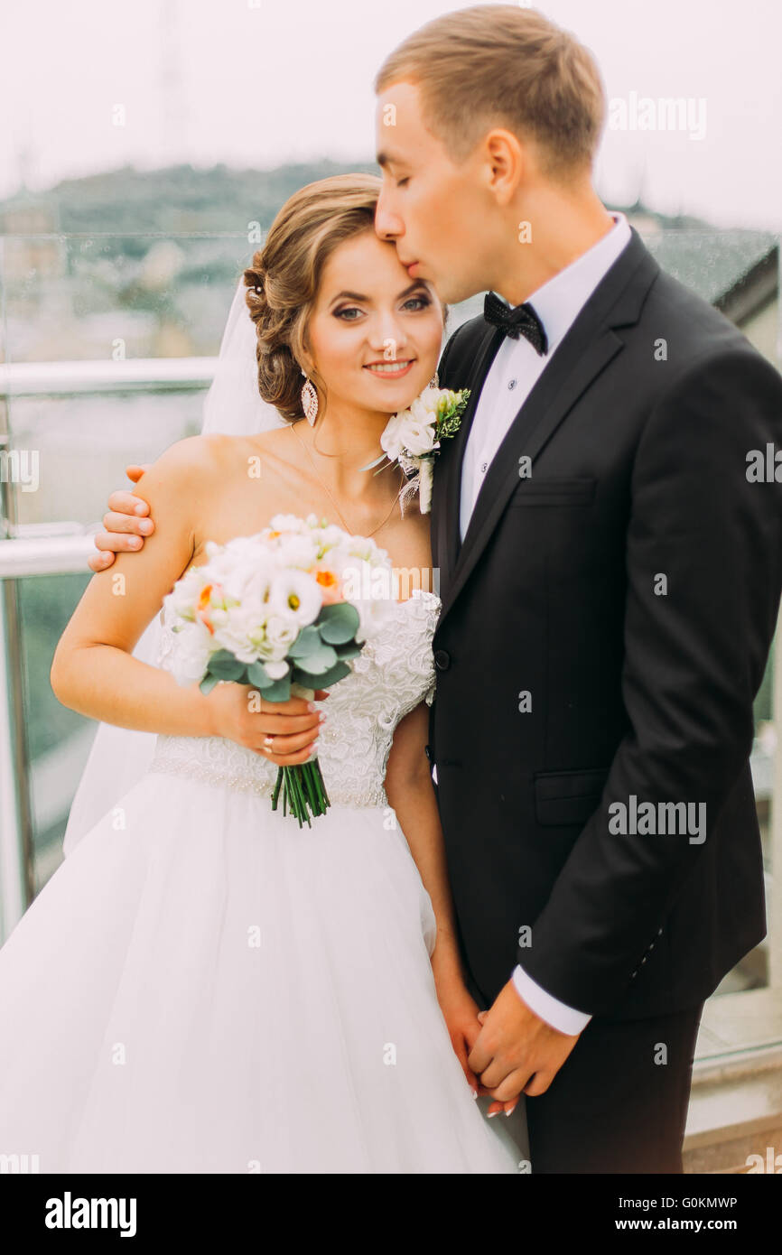 Happy beautiful couple, groom kissing bride forehead on the terrace ...