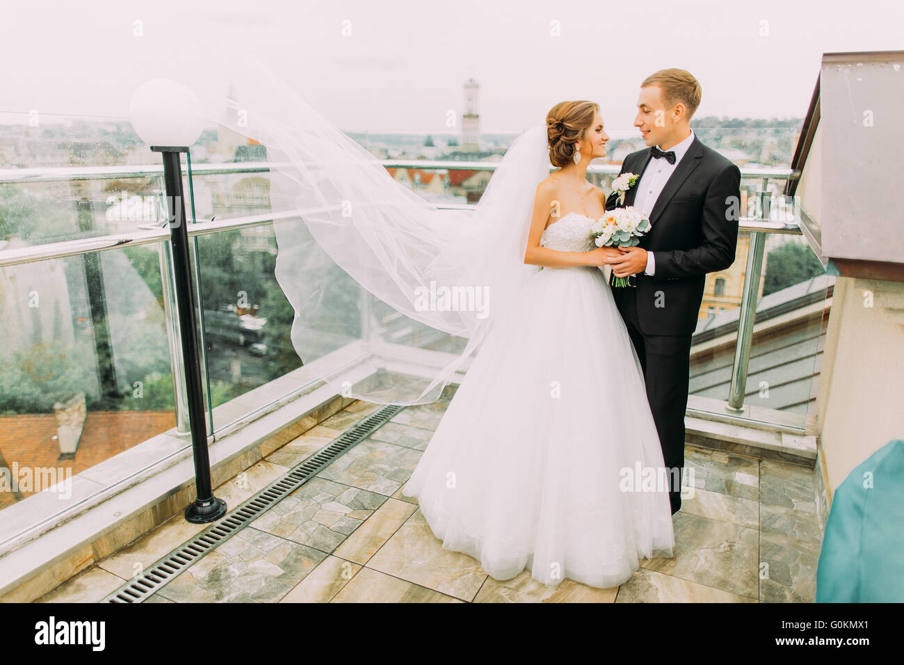 Happy bride and groom softly hugging on the terrace with cityscape ...