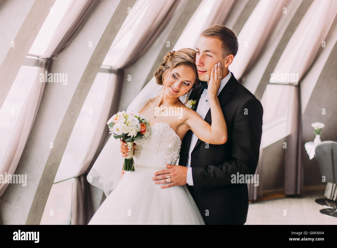 Beautiful happy bride softly touches face of her groom on the luxurious ...