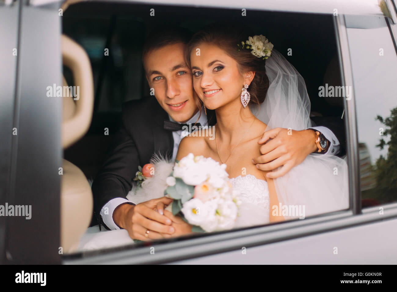 Happy beautiful groom and bride with bridal bouquet, hairstyle in car ...