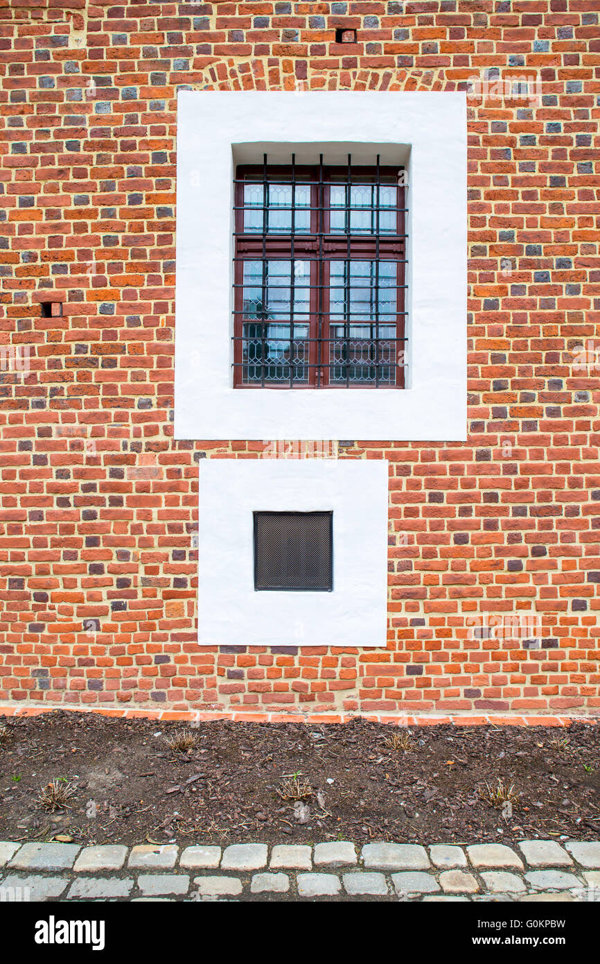 Two old square windows, one with steel grating. Old red brick wall ...