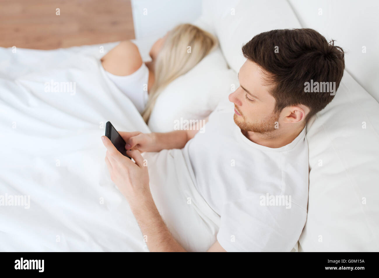 man texting message while woman is sleeping in bed Stock Photo - Alamy
