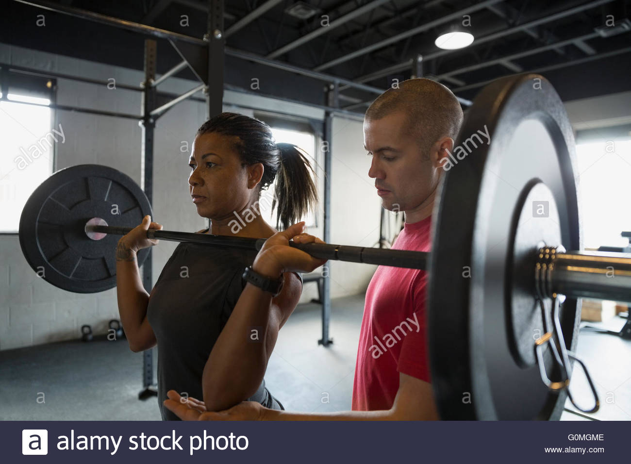 Personal trainer guiding woman weightlifting barbell Stock Photo - Alamy