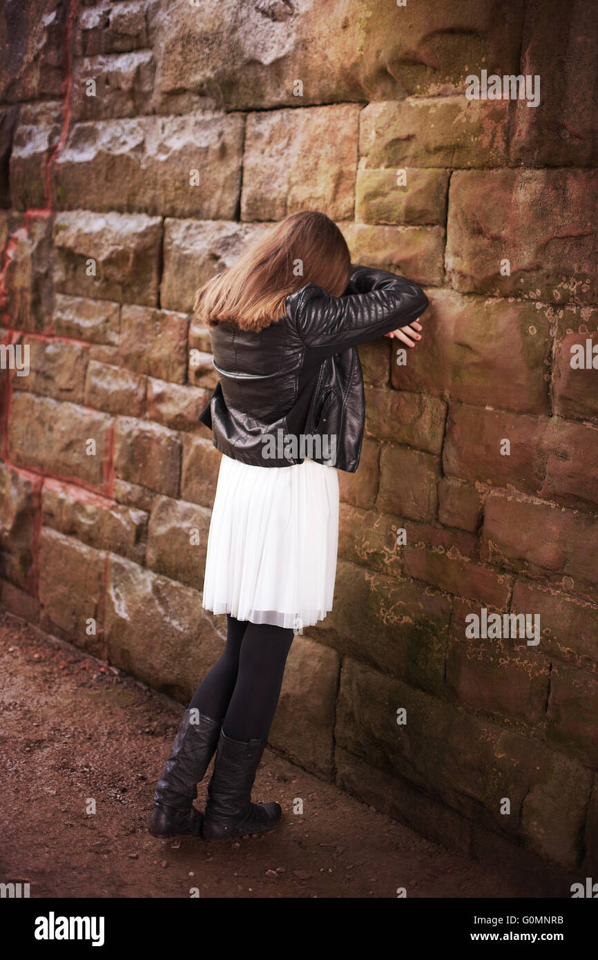 Back of a teenage girl leaning against a wall with her head in her ...