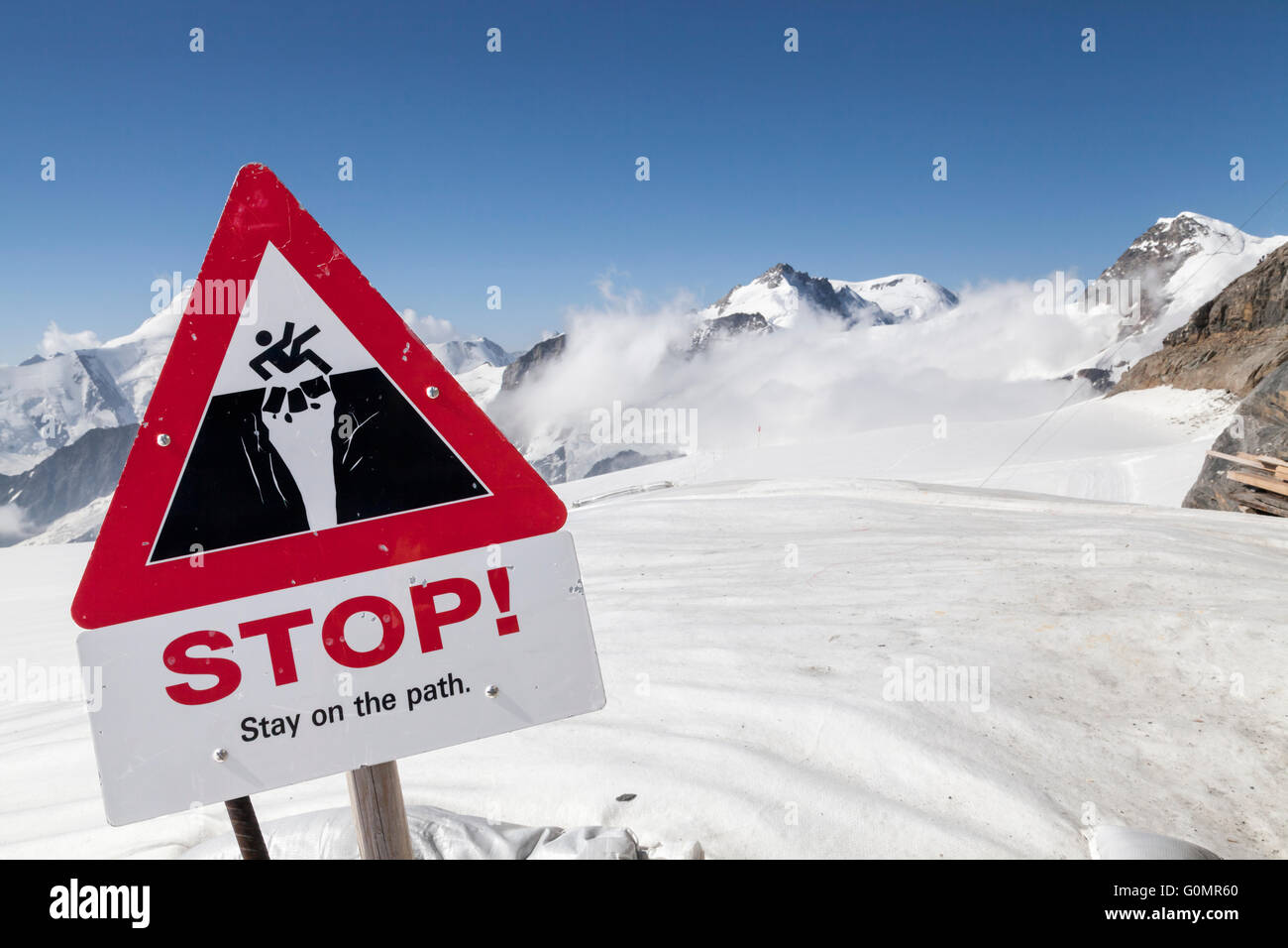 A 'Stop' sign on a snow capped mountain in Switzerland against a blue ...