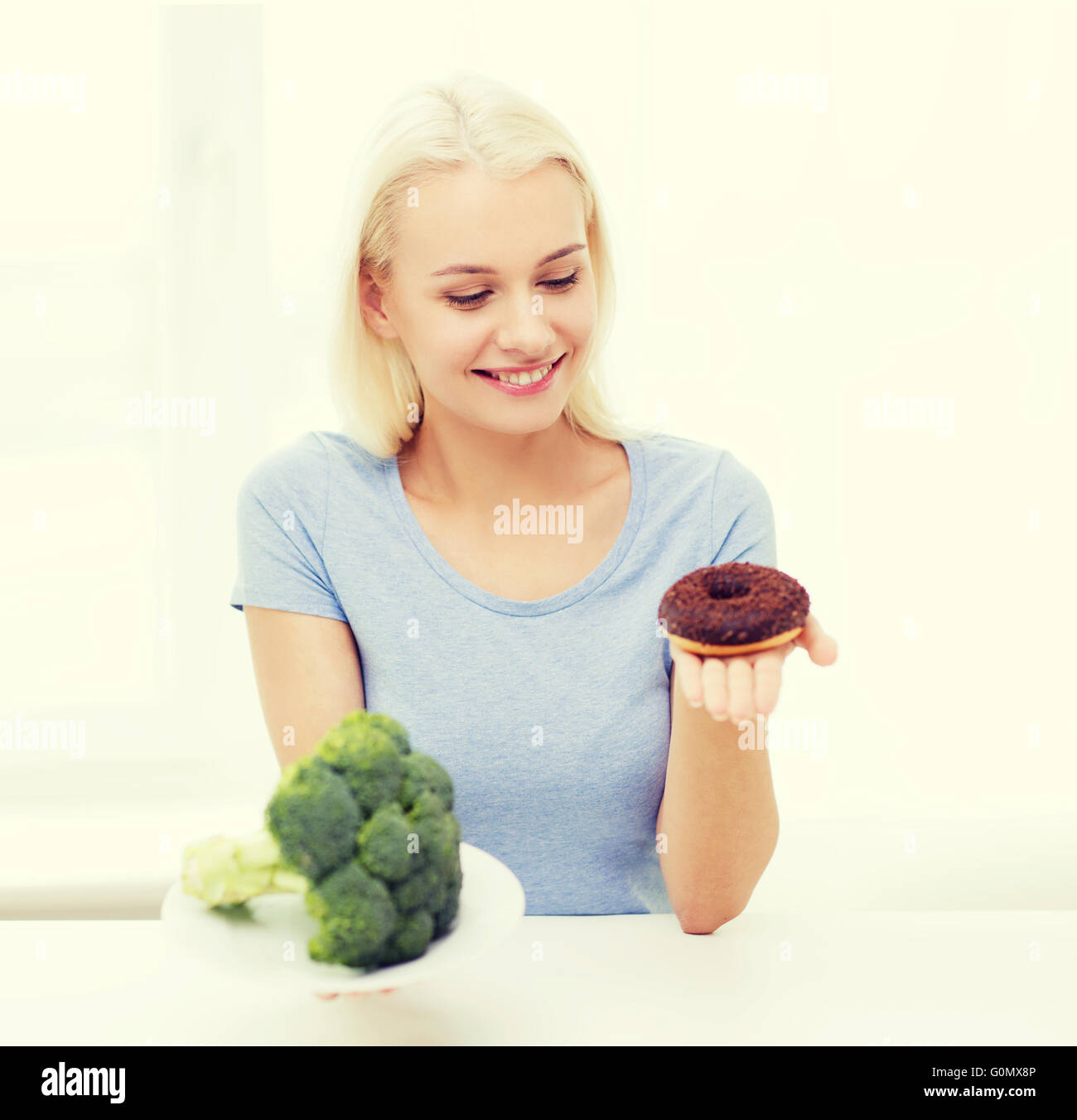 smiling woman with broccoli and donut at home Stock Photo - Alamy