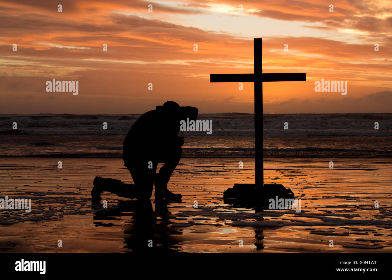 Man bowing down before a cross at sunset Stock Photo - Alamy