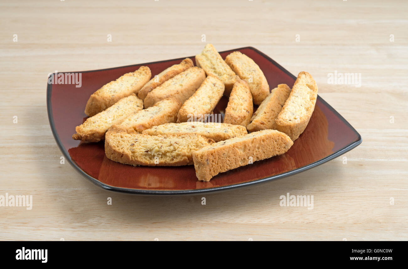Several almond nut biscotti on a maroon plate atop a wood table top ...