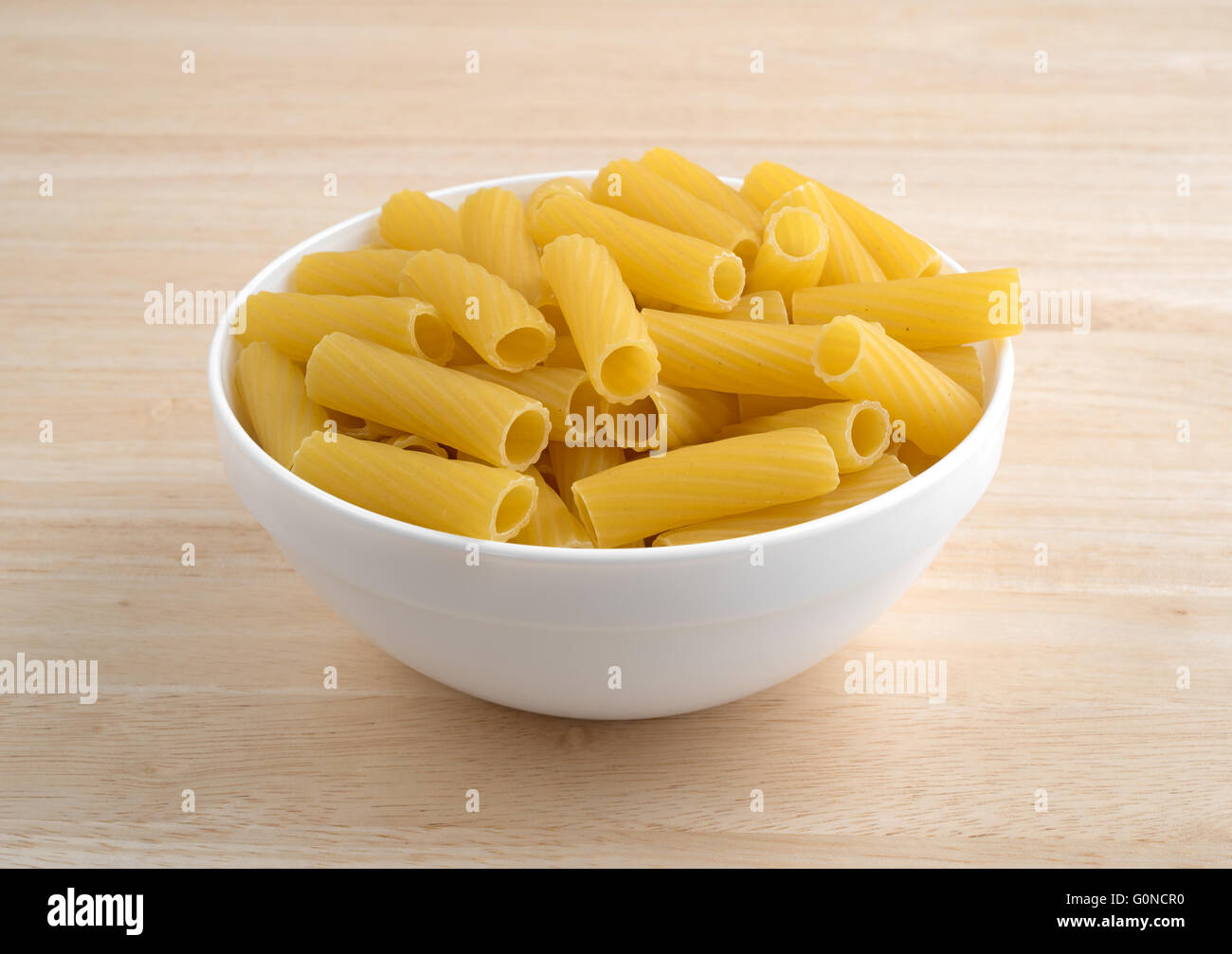 A small white bowl filled with rigatoni pasta on a wood table top Stock ...