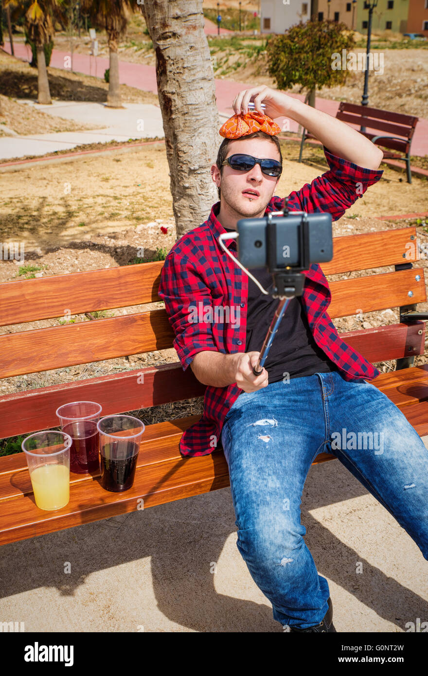 Guy documenting his hangover on a park bench with a selfie, a concept ...