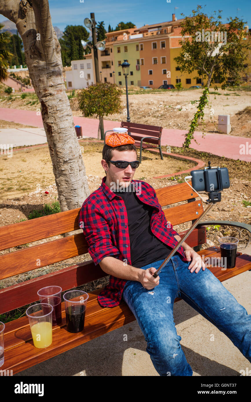 Guy documenting his hangover on a park bench with a selfie, a concept ...