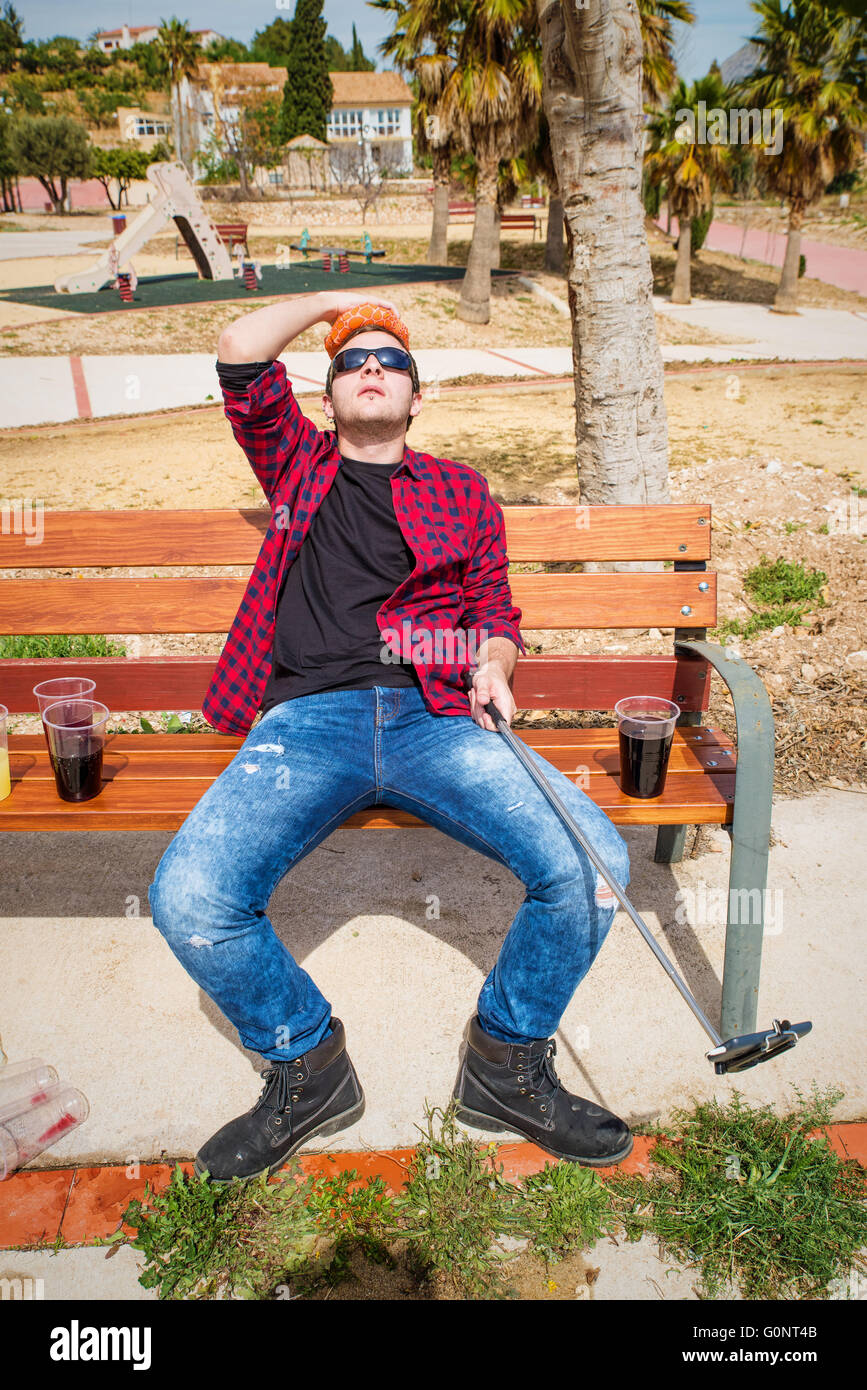 Guy documenting his hangover on a park bench with a selfie, a concept ...
