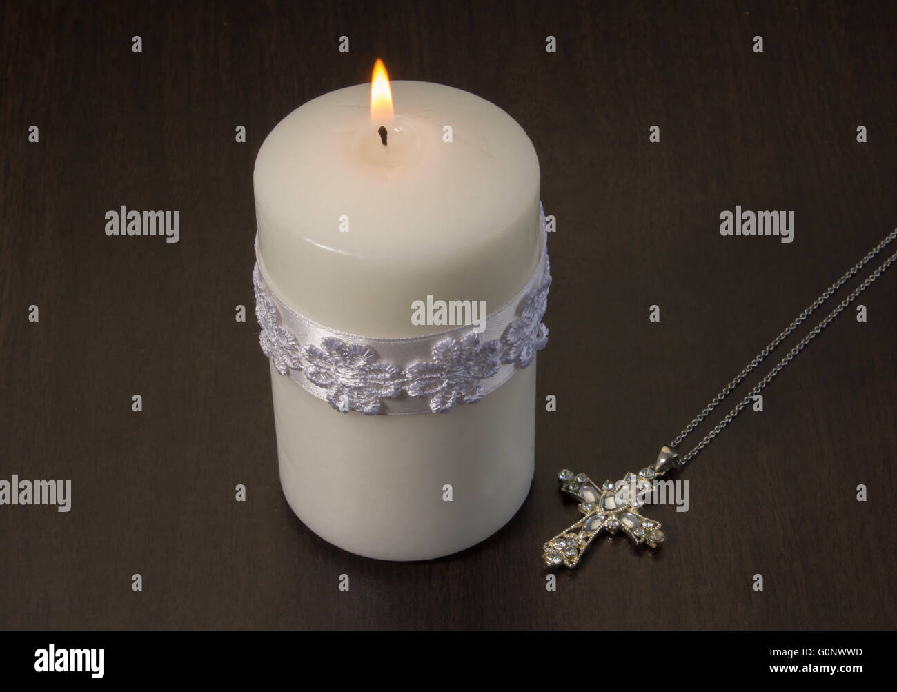 One white candle lit with pendant crystal cross on wood background ...