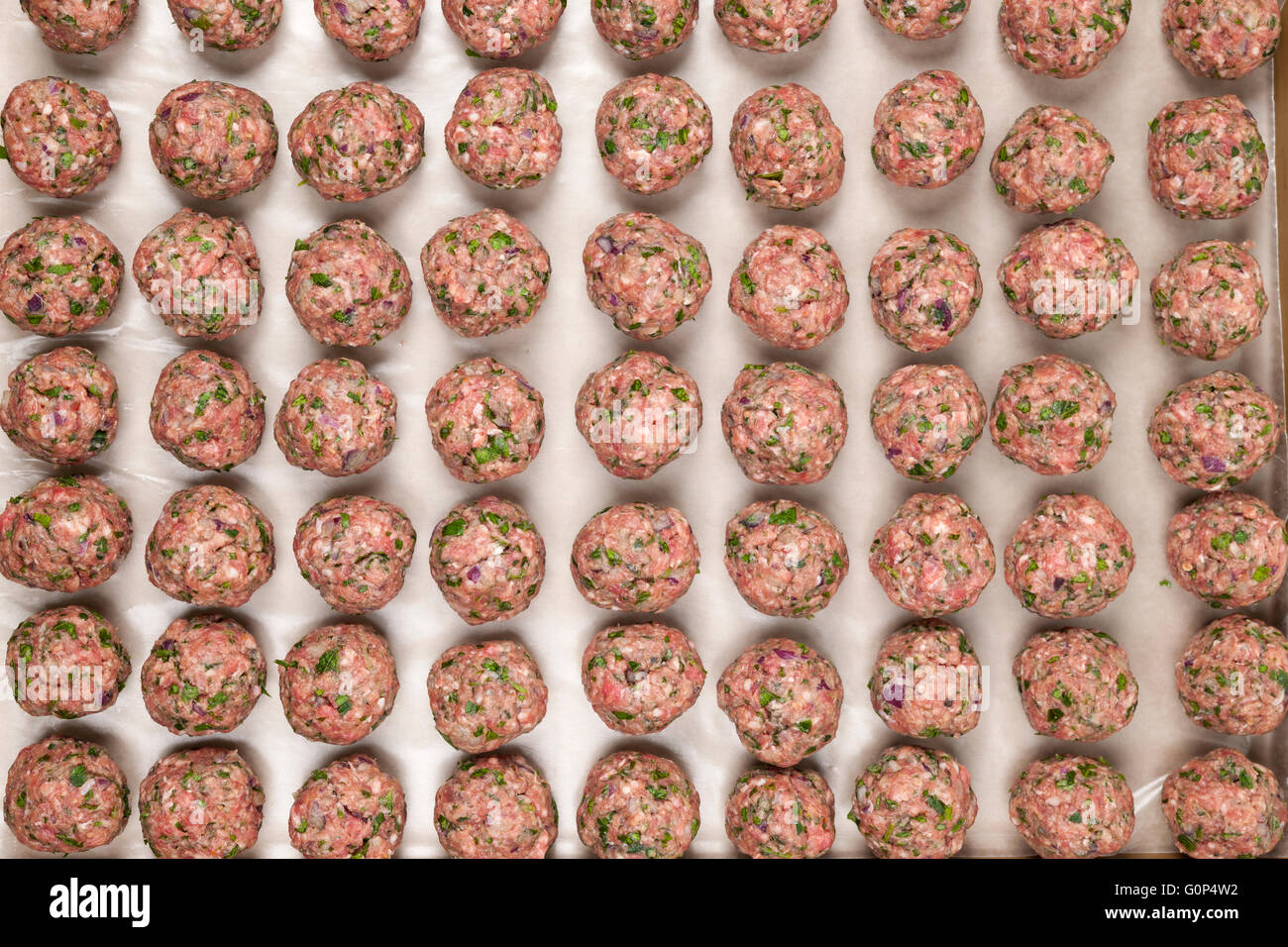 Rows of raw homemade meatballs prepared for cooking on a tray, overhead ...