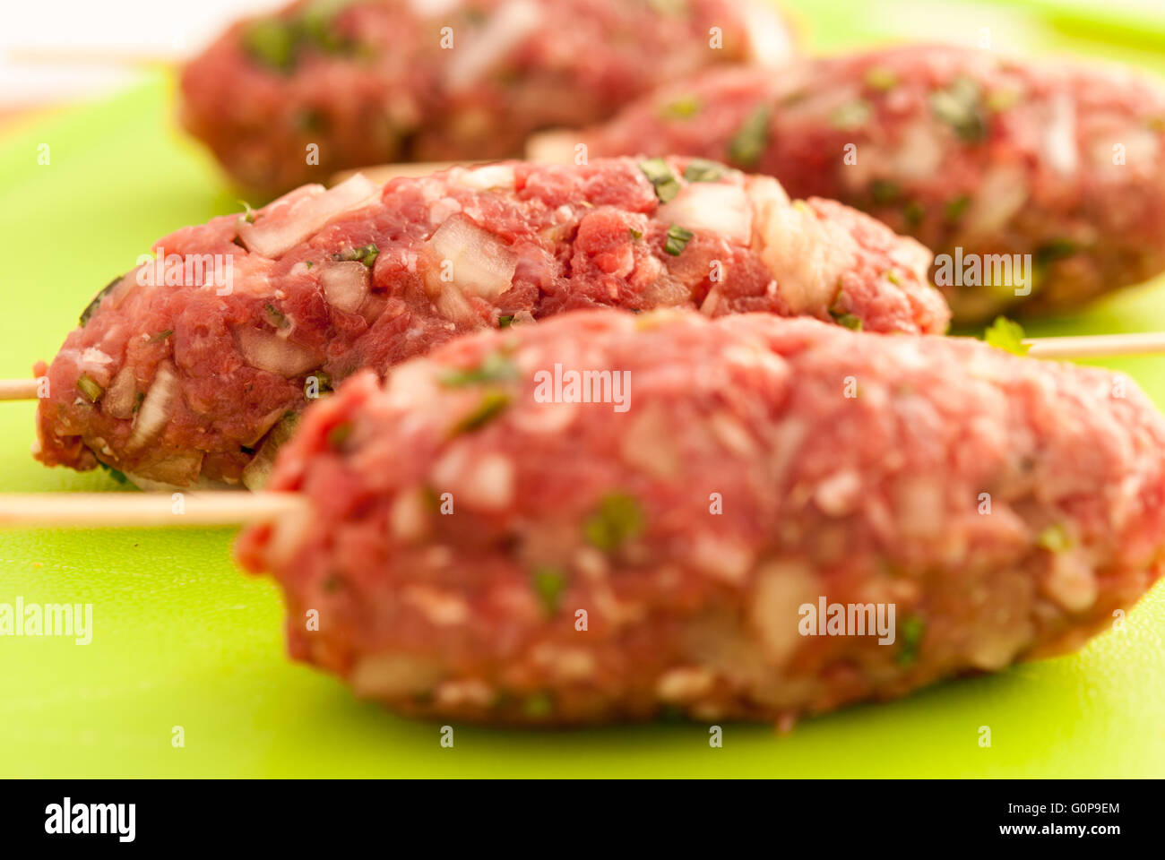 Raw beef kebab(kofta) on a wooden skewers on a green background closeup ...