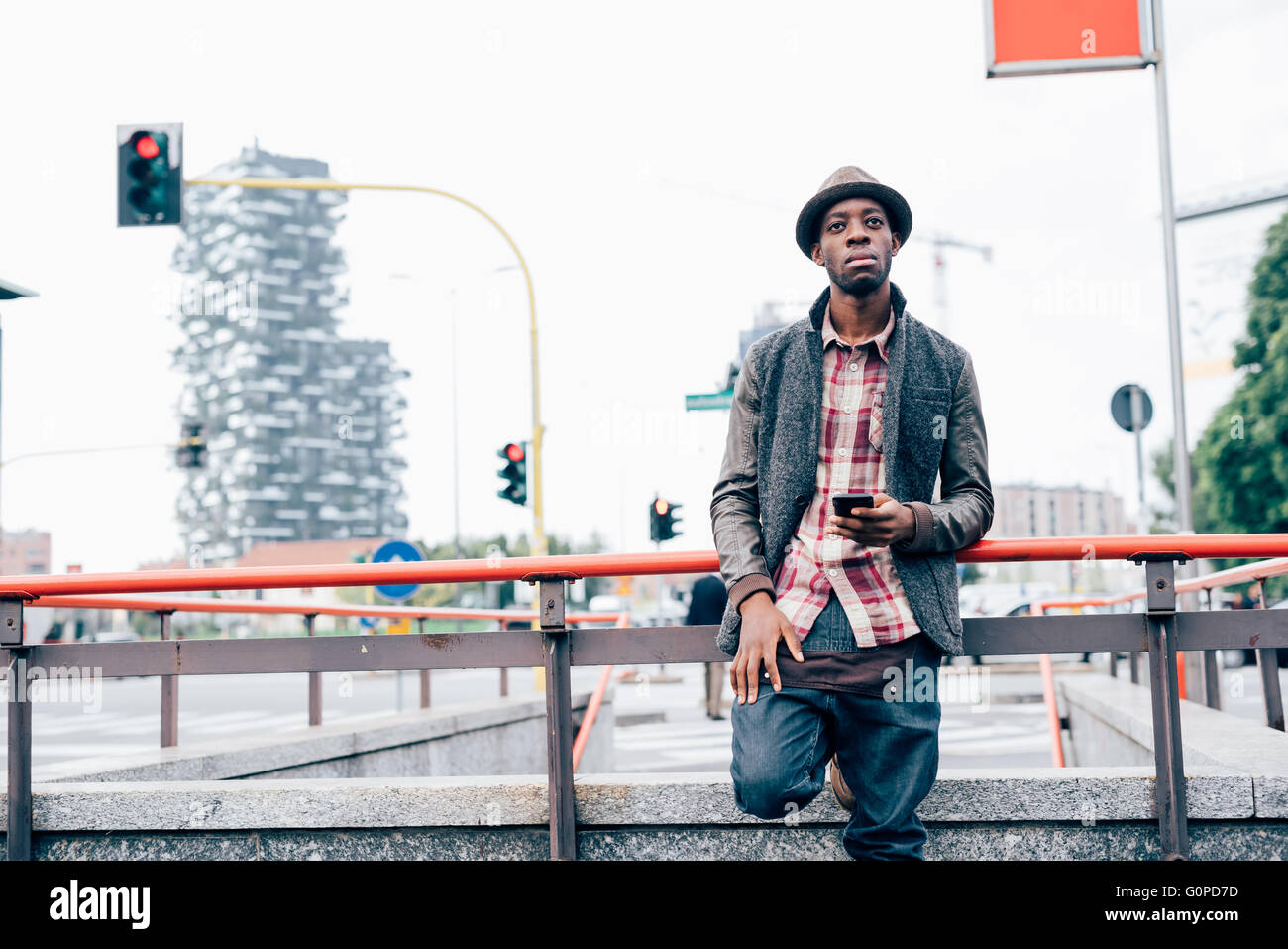 Knee figure of young handsome afro black man leaning on a handrail, holding a smart phone ...