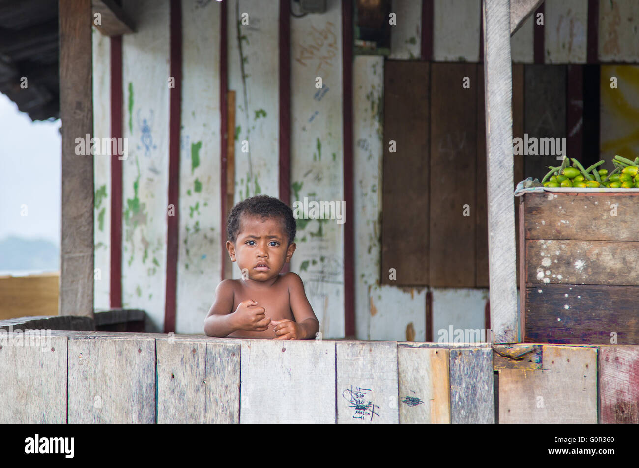small Papuan boy with a sad face at a porch of his house Stock Photo ...