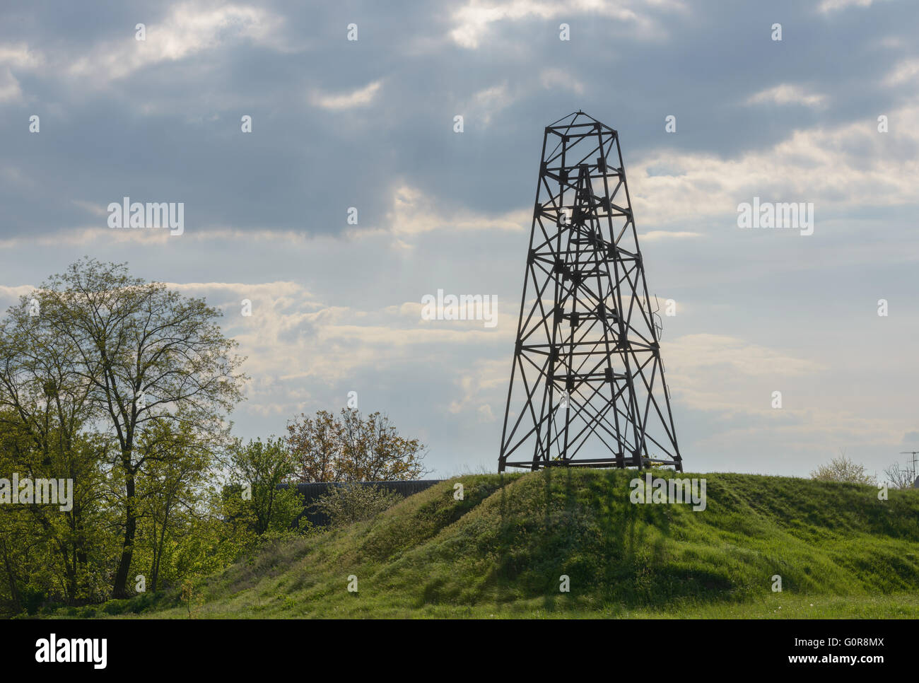 Silhouette of metal geodetic tower is on hillock on cloudy sky ...