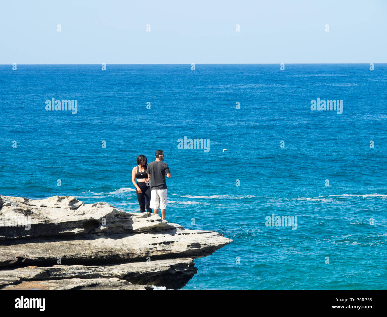 A couple standing on the edge of a rocky ledge overlooking the Pacific ...