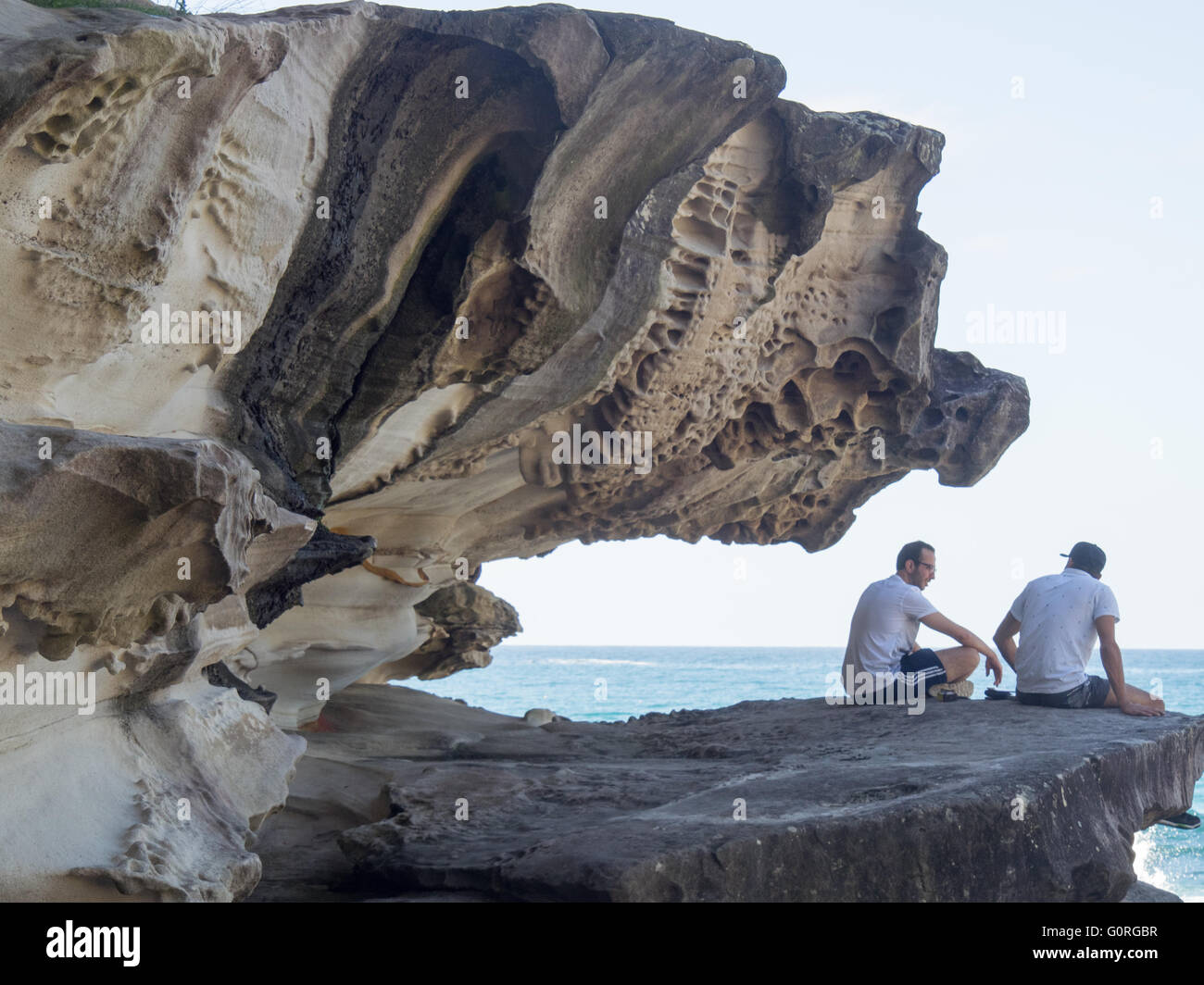 Two men sitting on a rocky ledge on the Coastal Walk path south of ...