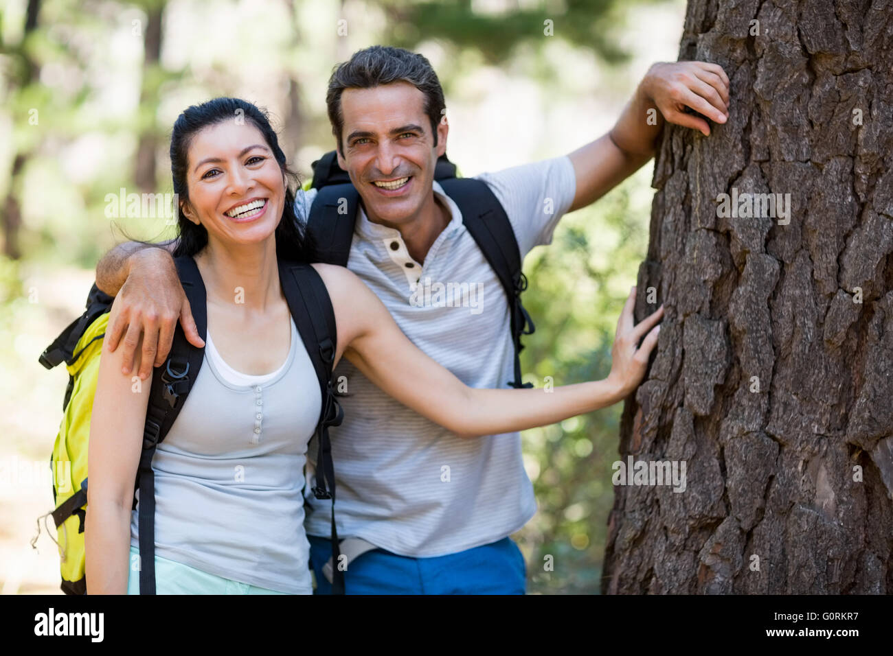Couple smiling and resting against a tree Stock Photo - Alamy