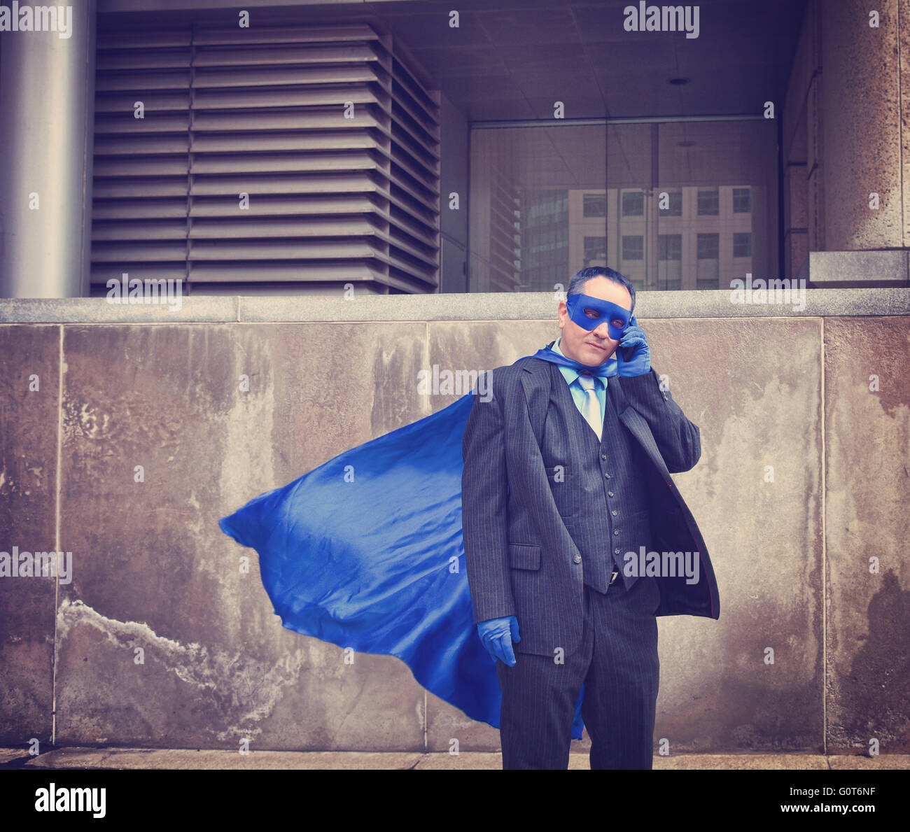 A business man is dressed up as a super hero using a phone in the city ...