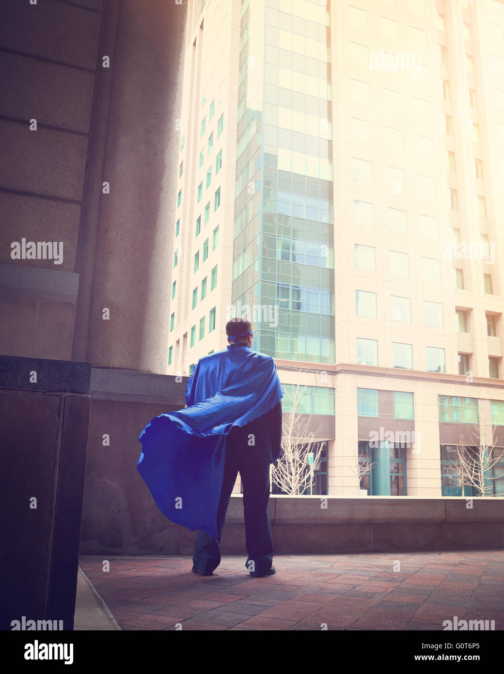 A business man wearing a super cape is standing in a city for a success ...