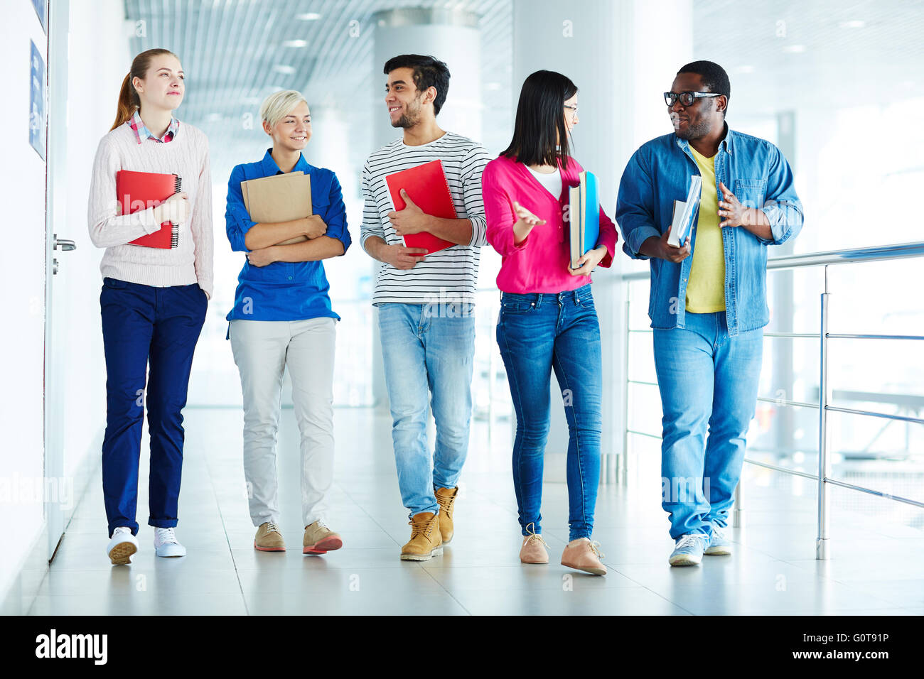 Group of college learners with books walking down corridor and talking ...
