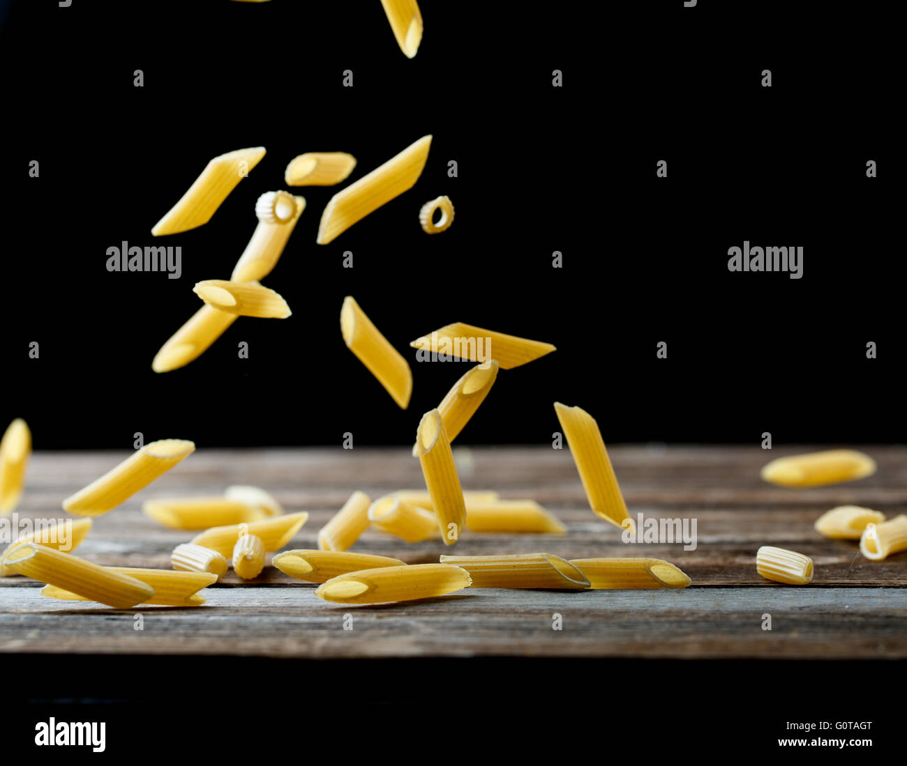 Falling penne pasta. Flying yellow raw macaroni over black background ...