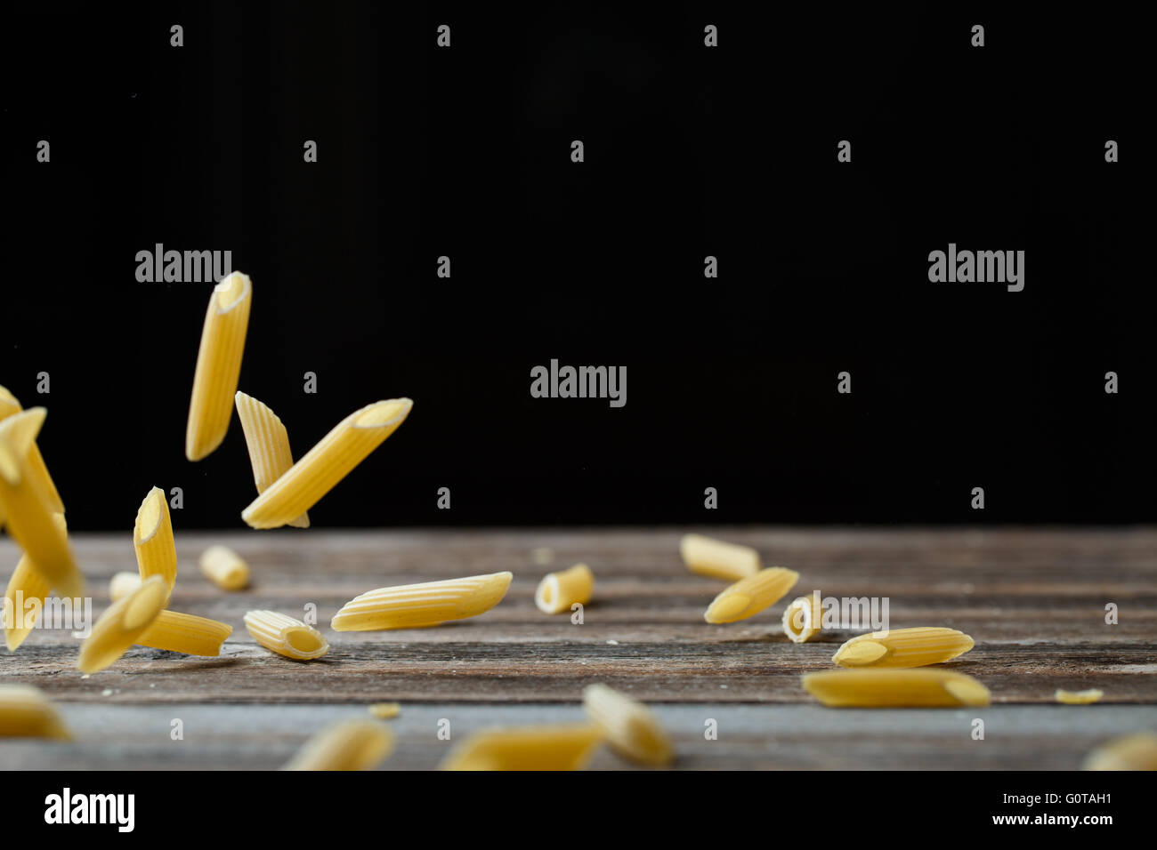 Falling penne pasta. Flying yellow raw macaroni over black background ...