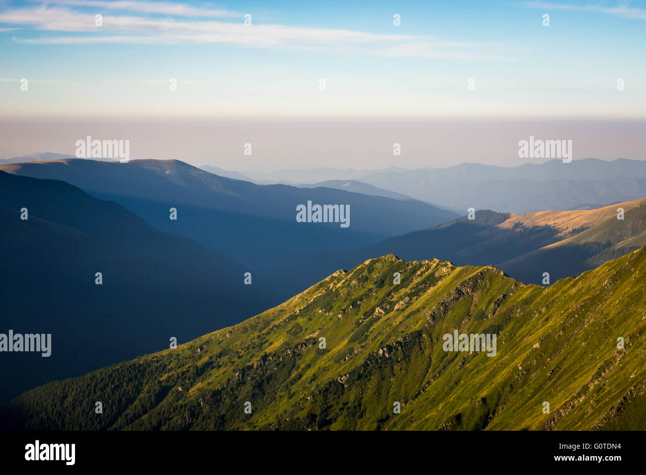 Mountainside with green grass, other mountain ranges in shadow and fog ...