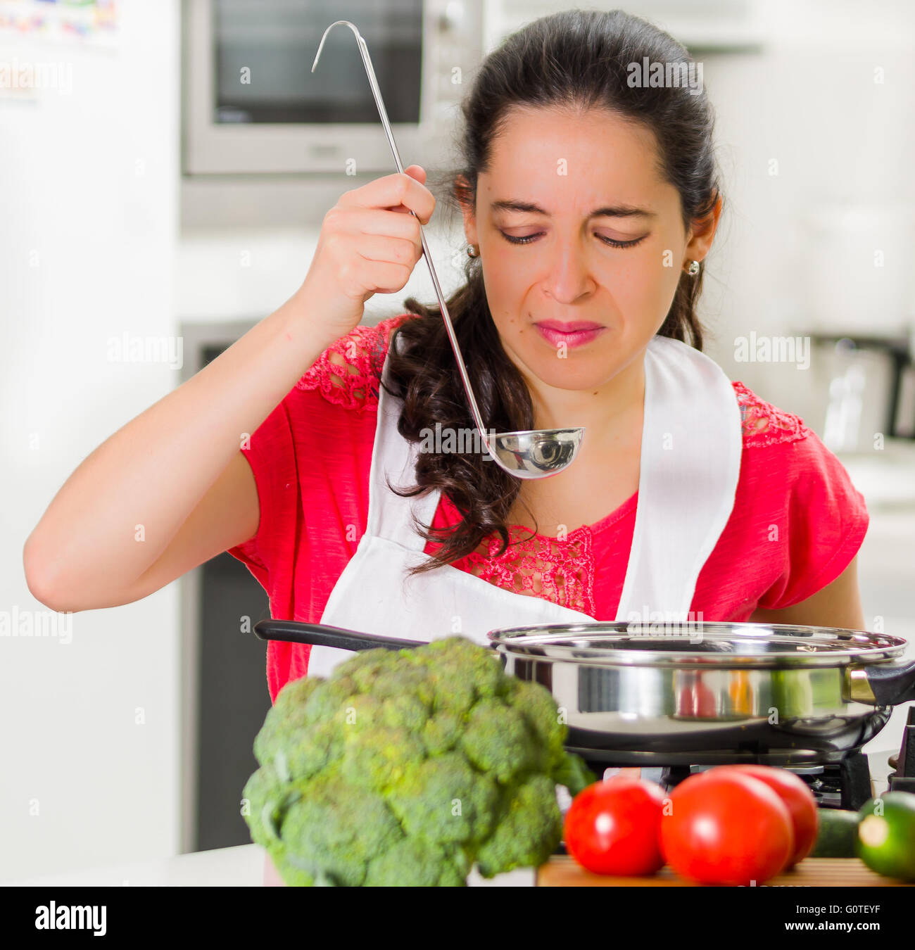 Young woman chef tasting food from kettle with skeptical facial ...