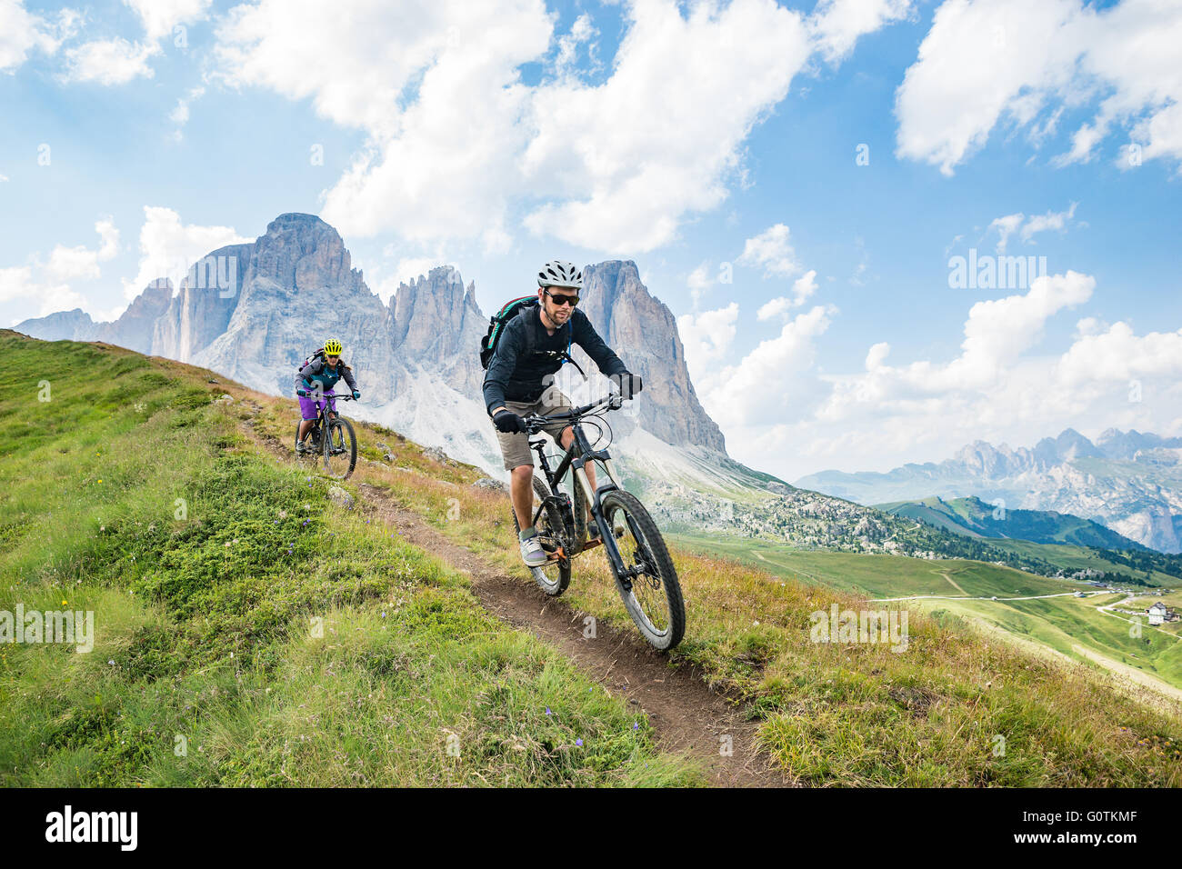 A man and a woman on mountain bikes racing along trail in the Dolomites ...