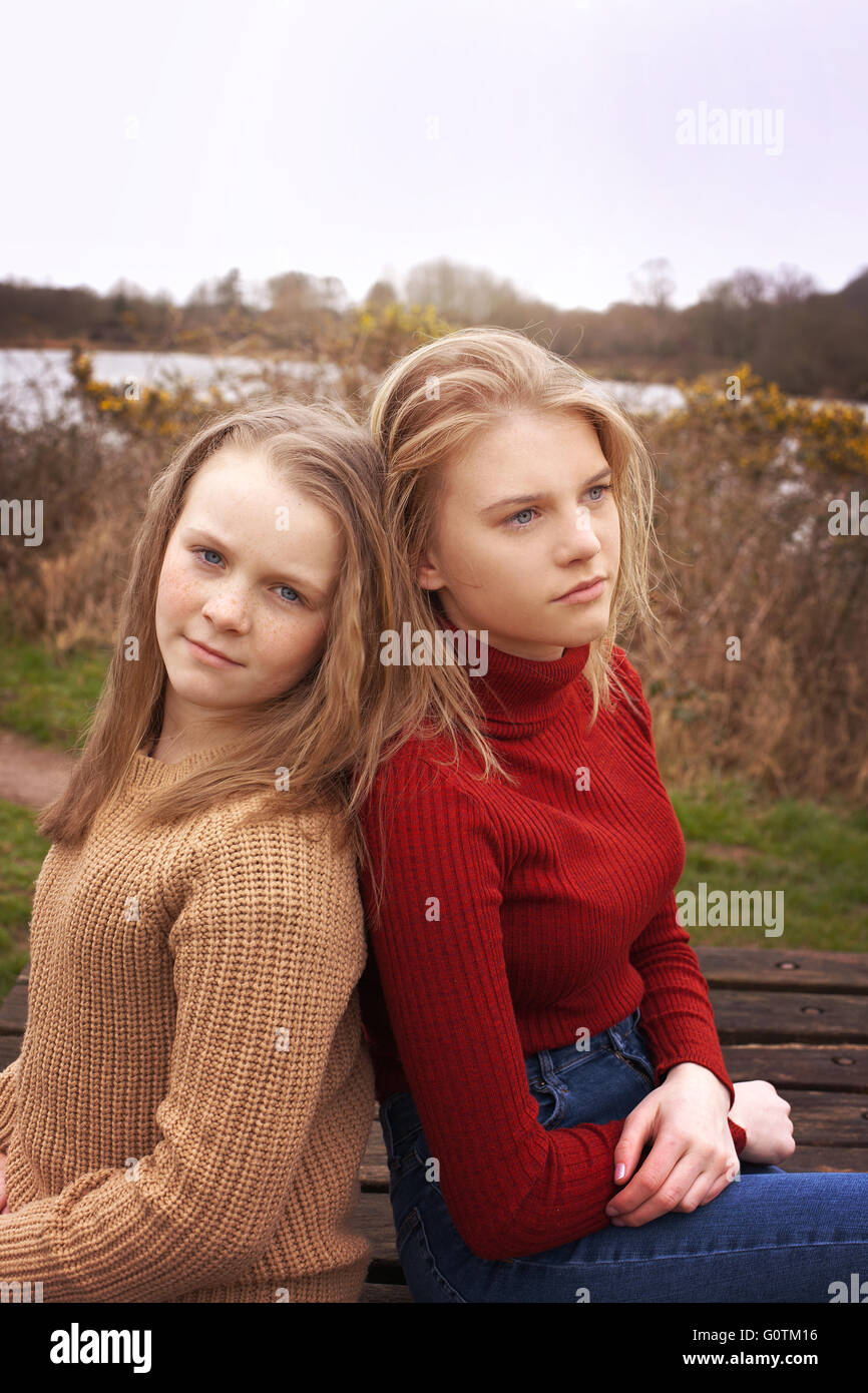 Two sisters sitting back to back in an outdoor setting Stock Photo - Alamy