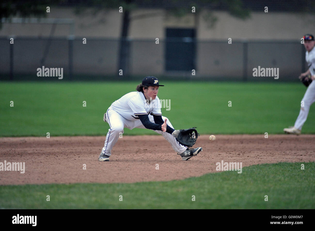 A high school third baseman fielding a ground ball wide of the bag ...