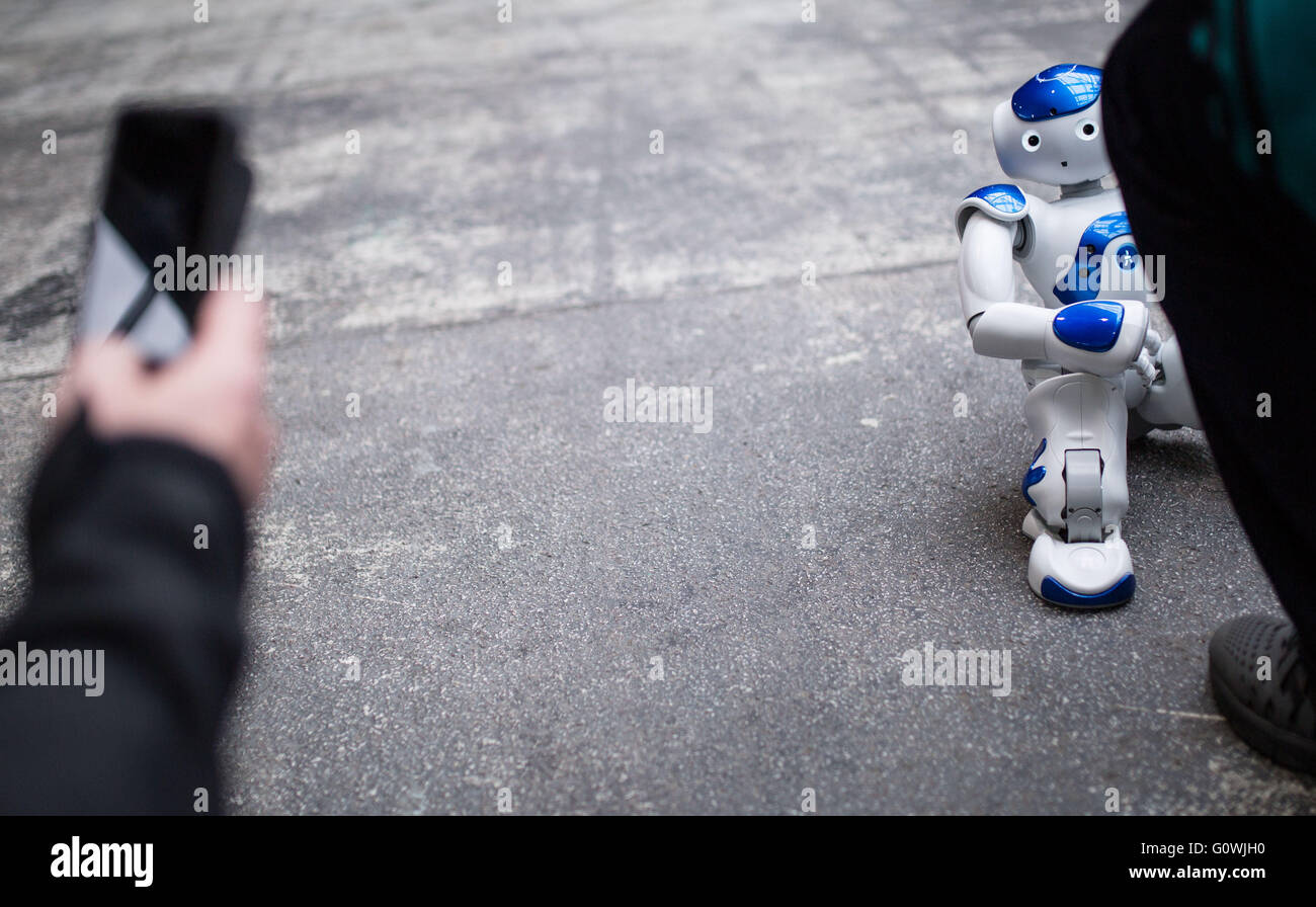 A man photographs a programmable robot, hiding behind a man's leg, with ...