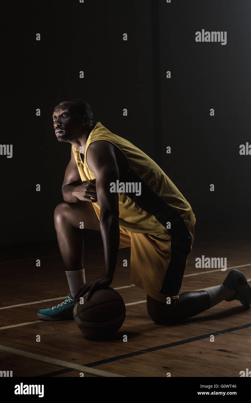 Portrait of basketball player with a knee on the floor and a hand on ...