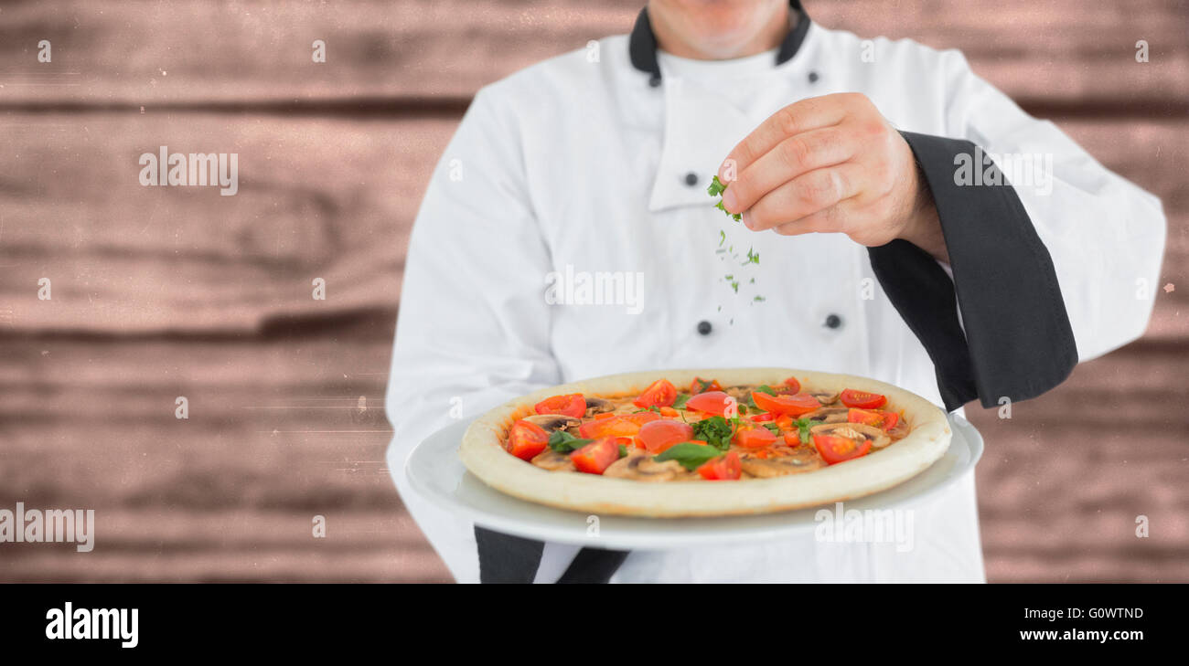 Composite image of portrait of a chef holding a pizza and adding herbs ...